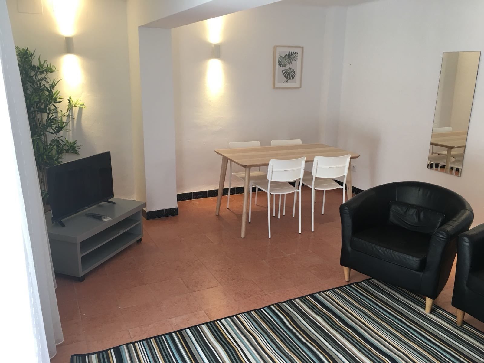 Uma sala de estar moderna com televisão, mesa de jantar com cadeiras, poltrona de couro preta e tapete listrado.
