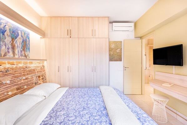 Quarto com cama, guarda-roupa de madeira, televisão e obras de arte.