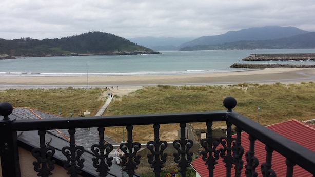 Vista costeira a partir de uma varanda com grade, uma praia e uma montanha ao longe.