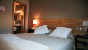 Quarto de hotel com uma cama grande, cabeceira de madeira, mesa de cabeceira com abajur e um espelho.