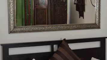 Cama com roupa de cama branca e almofadas decorativas, cabeceira escura e um espelho grande e ornamentado acima.