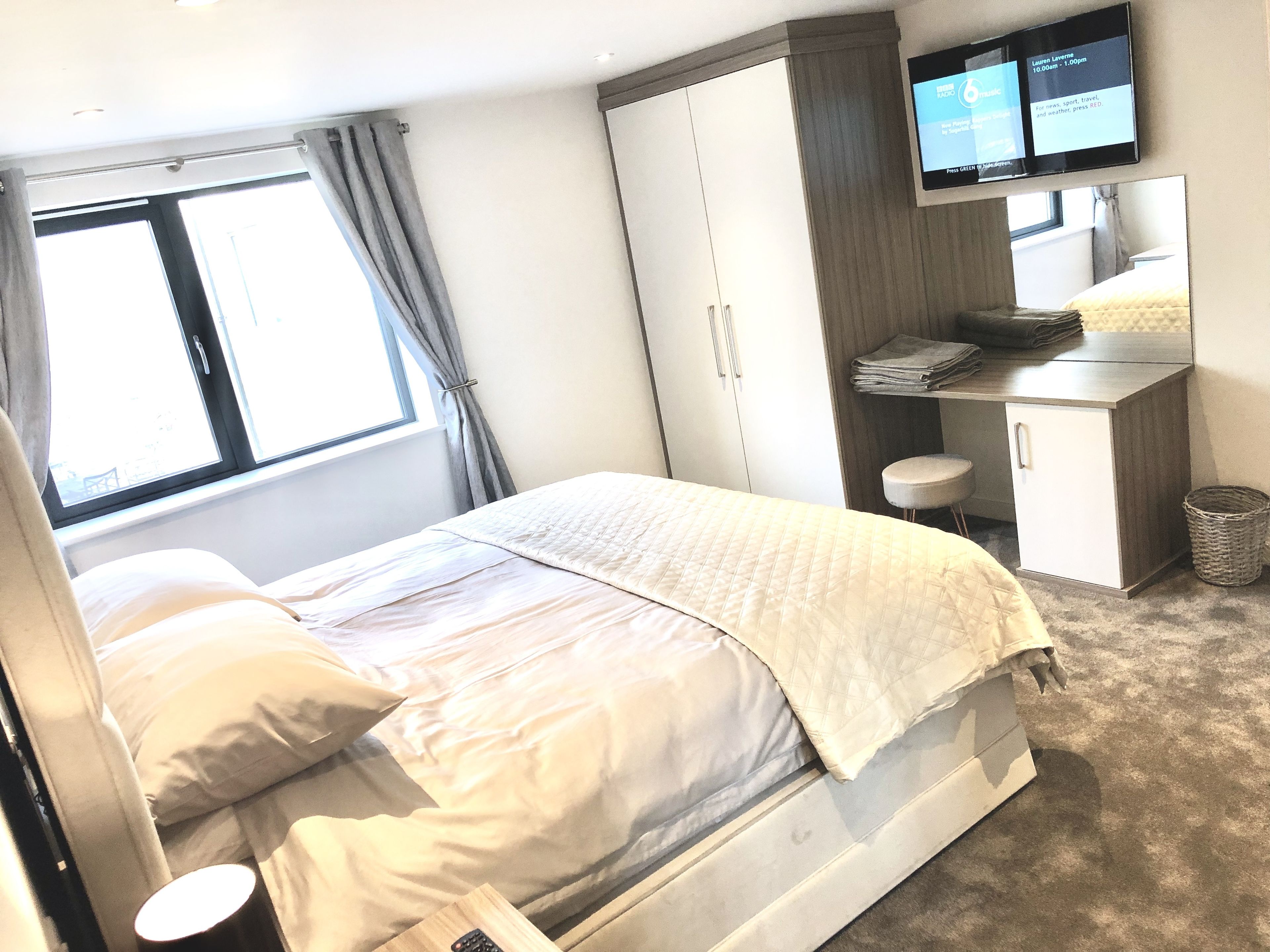 Quarto de hotel com cama, escrivaninha, televisão e janela.