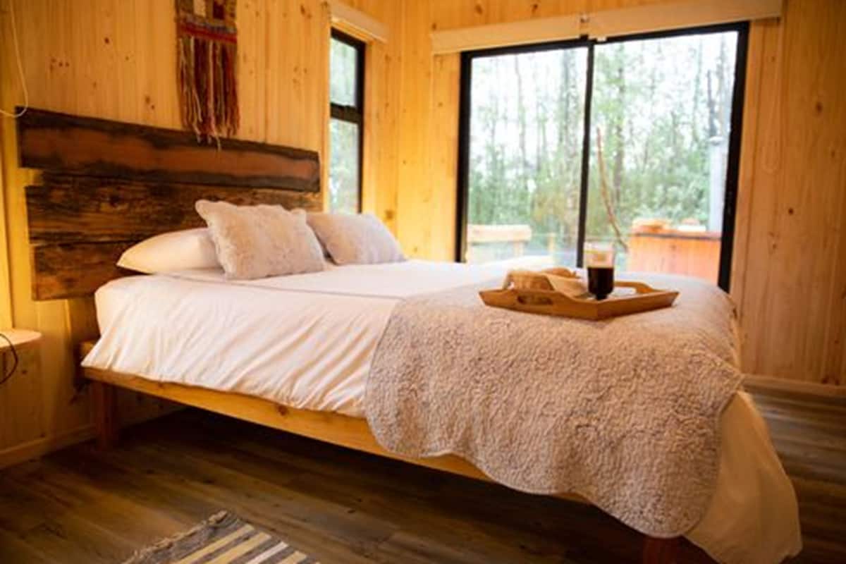 Quarto de cabana de madeira com uma cama, um tabuleiro com uma xícara e uma janela grande.