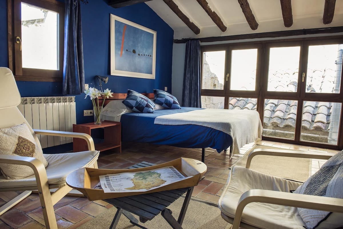 Quarto com uma cama, uma cadeira, uma mesa com um mapa e uma janela com vista para o exterior.