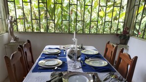 Uma mesa de jantar posta com pratos, talheres e guardanapos, com uma estátua e planta em vasos ao fundo.