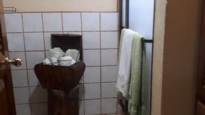 Um banheiro pequeno com uma pia de madeira, um porta-toalhas com uma toalha verde, um quadro na parede e um tapete de chão com estampas de palmeiras.