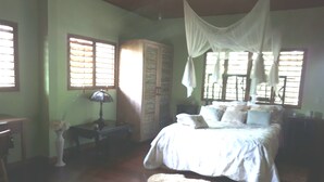 Quarto com cama, mesa de cabeceira, luminária, guarda-roupa e janela com cortina.