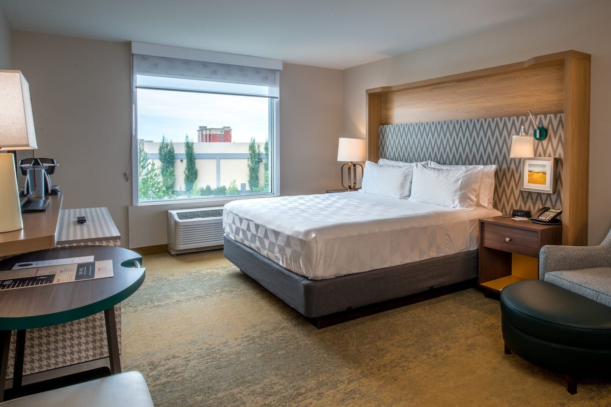 Quarto de hotel com uma cama grande, uma escrivaninha, uma cadeira e vista para a cidade.