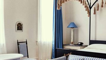 Quarto com sofá estampado xadrez, mesa redonda de madeira com um vaso, banheira branca, uma cadeira, cama com cabeceira metálica e um candelabro.
