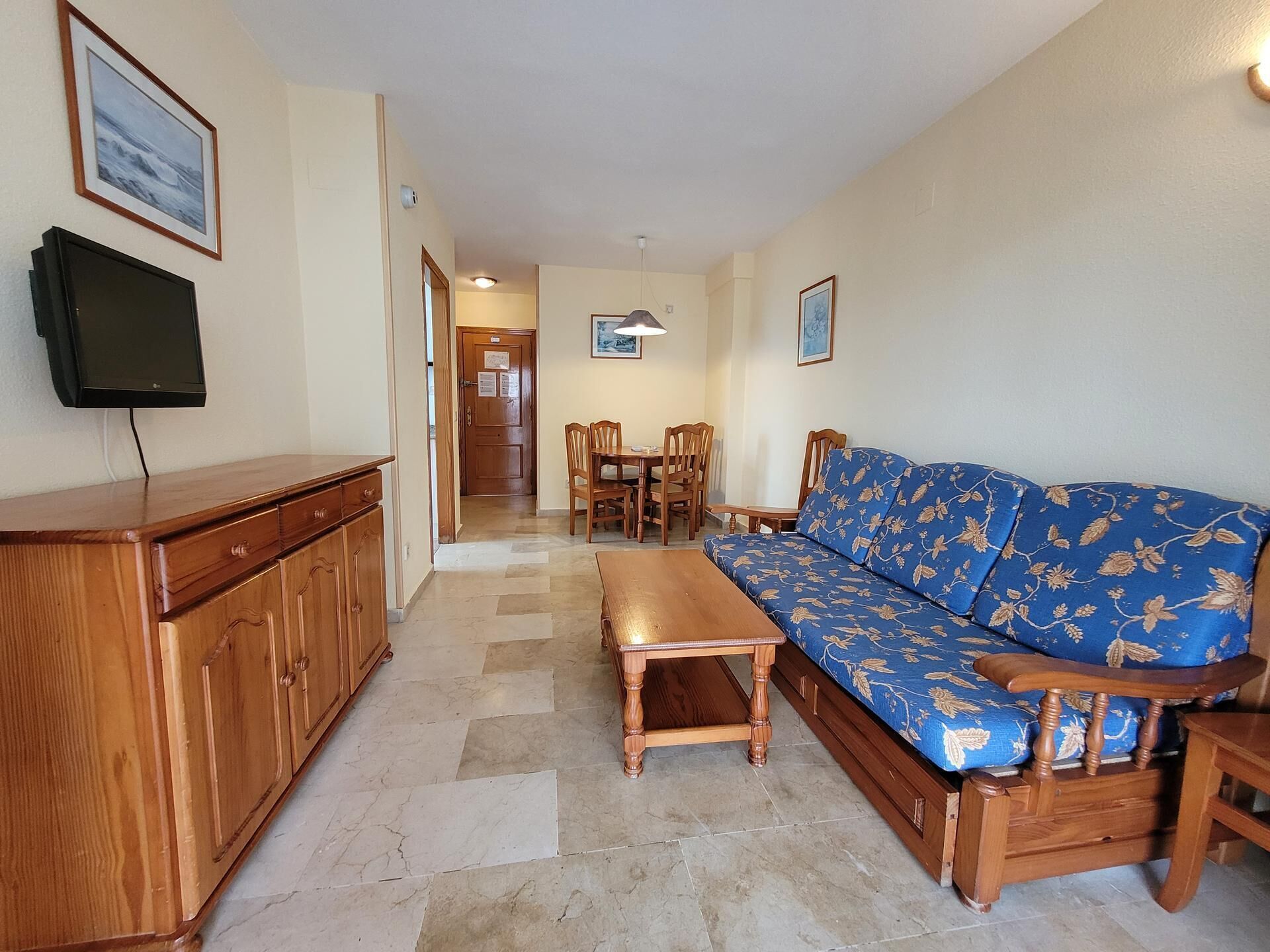 Uma sala de estar com sofá, aparador de madeira, televisão e um espaço de jantar com cadeiras e mesa.