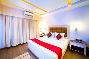 Quarto de hotel com uma cama grande, mesa de cabeceira com luminária, telefone e aparelho de ar condicionado.