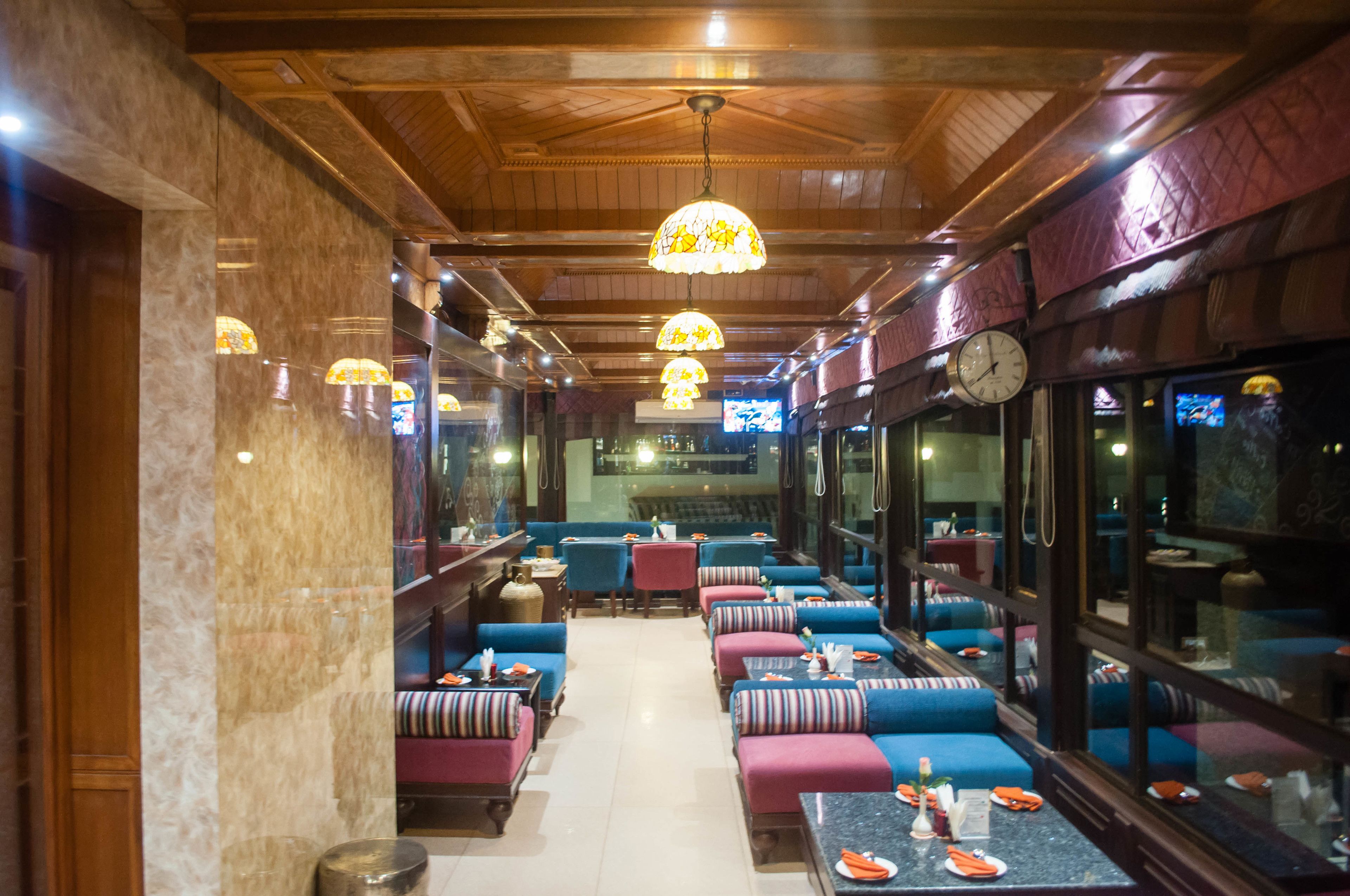 Um restaurante com cabines e mesas, teto de madeira e luminárias pendentes.