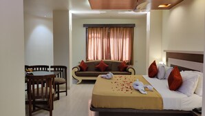 Quarto de hotel com cama, sofá, mesa de jantar com cadeiras e janela com cortinas.