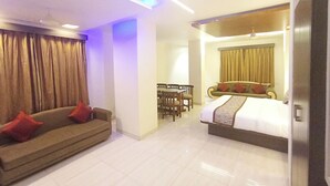 Quarto de hotel com cama, sofá, mesa de jantar com cadeiras e um espaço de refeições separado.
