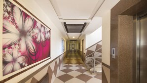 Um corredor com piso xadrez, um grande quadro floral na parede e uma escada com corrimão de metal.