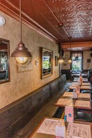 Interior de restaurante com assentos em cabines de madeira, luminárias pendentes, obras de arte emolduradas nas paredes e cardápios sobre as mesas.