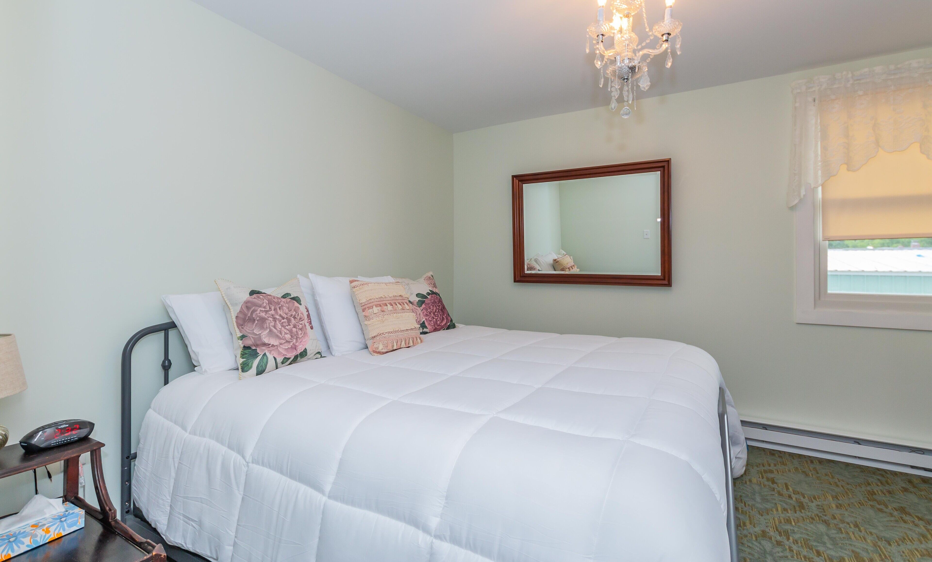 Quarto com cama, mesa de cabeceira, espelho e janela com cortina.