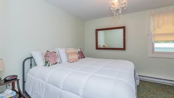 Quarto com cama, mesa de cabeceira, espelho e janela com cortina.