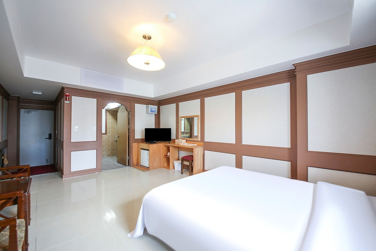 Quarto de hotel com cama, escrivaninha com televisão, espelho e chuveiro.