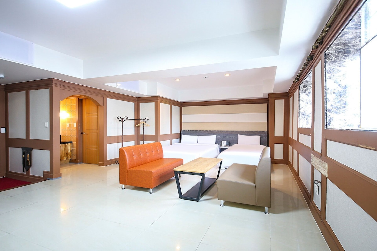 Quarto de hotel moderno com uma cama grande, um sofá laranja, uma mesinha e um guarda-roupa.