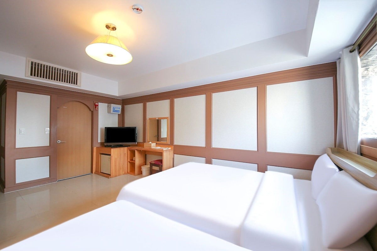 Quarto de hotel com uma cama, uma escrivaninha com televisão, um espelho e uma janela com cortinas.