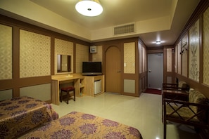 Quarto com duas camas, uma escrivaninha, televisão, mini-frigorífico e porta de madeira.