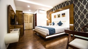 Quarto de hotel moderno com uma cama grande, piso de madeira, espelho, escrivaninha e uma cadeira.