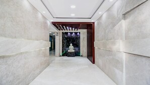 Um corredor de mármore com uma estátua de Buda ao centro, que leva a um quarto com parede de padrão escuro.