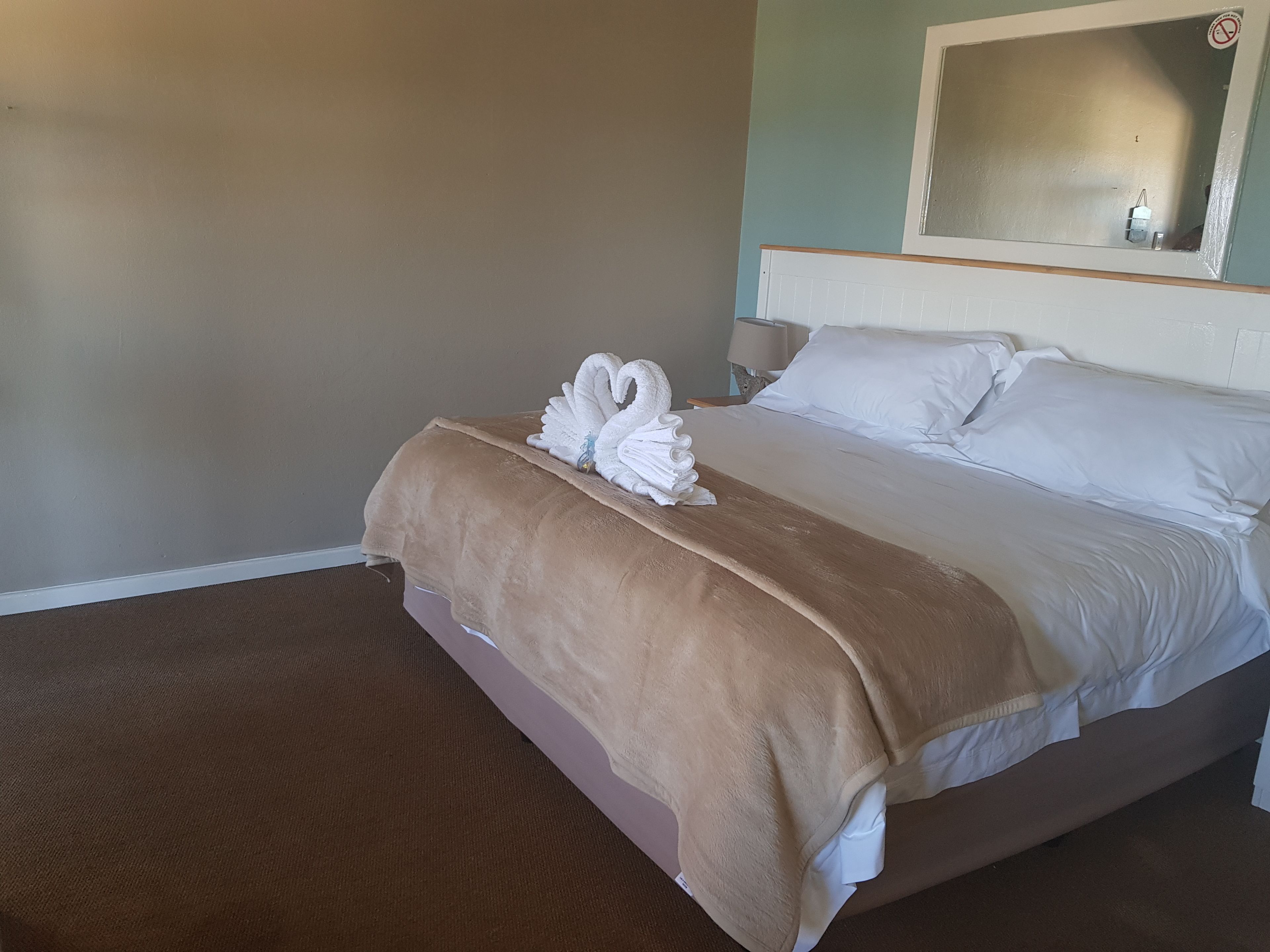 Quarto de hotel com uma cama, um cobertor marrom e uma toalha em forma de cisne sobre a cama.