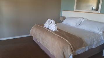Quarto de hotel com uma cama, um cobertor marrom e uma toalha em forma de cisne sobre a cama.