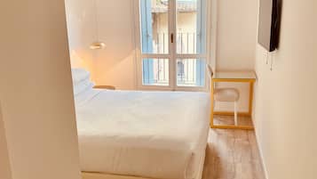 Quarto com cama, escrivaninha, cadeira, televisão e varanda com vista.