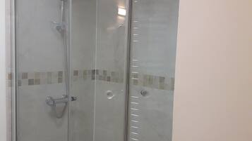 Box de chuveiro com paredes de vidro, piso ladrilhado e chuveiro.