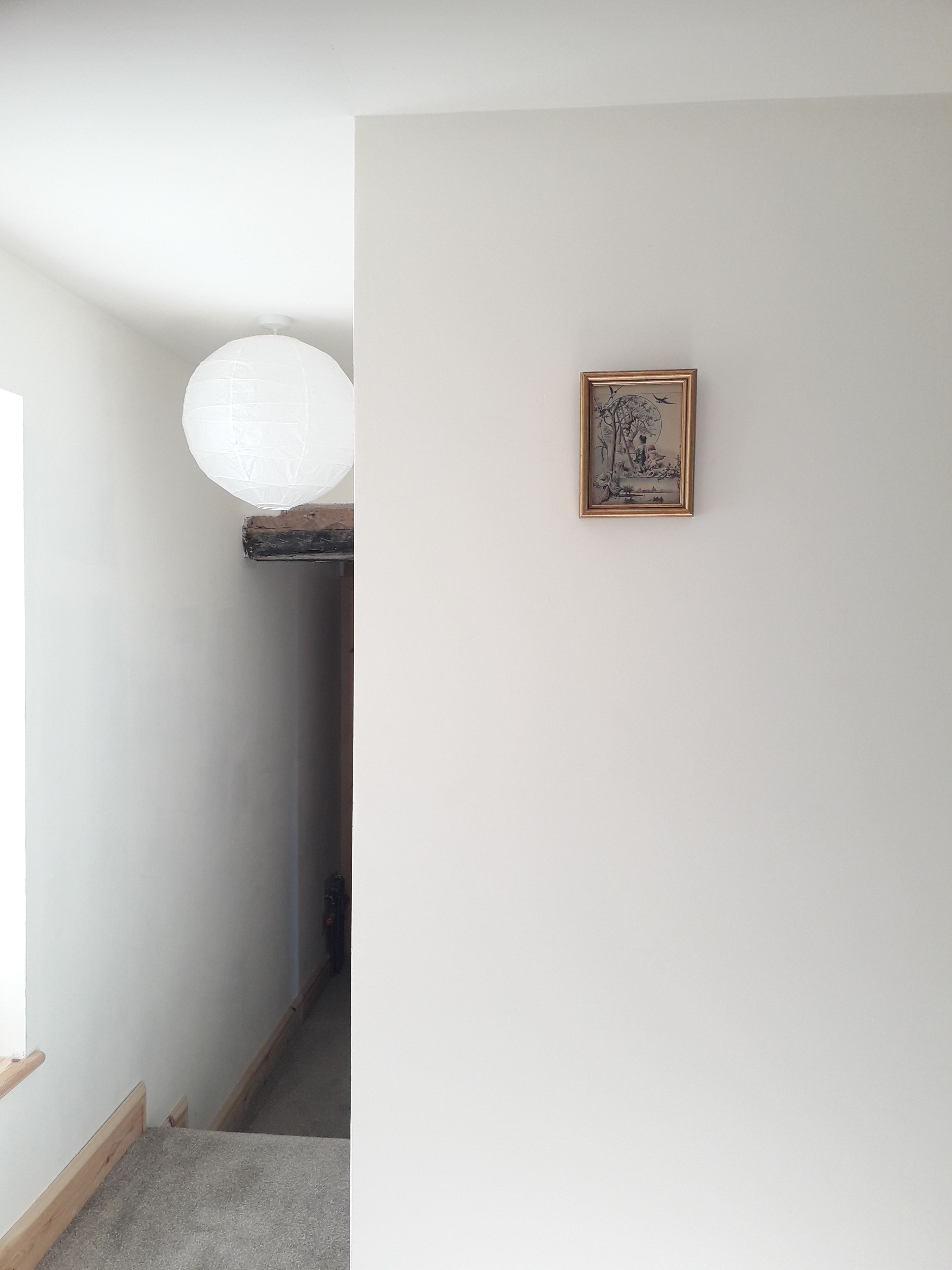 Um corredor com parede branca, um quadro emoldurado e um candeeiro suspenso.