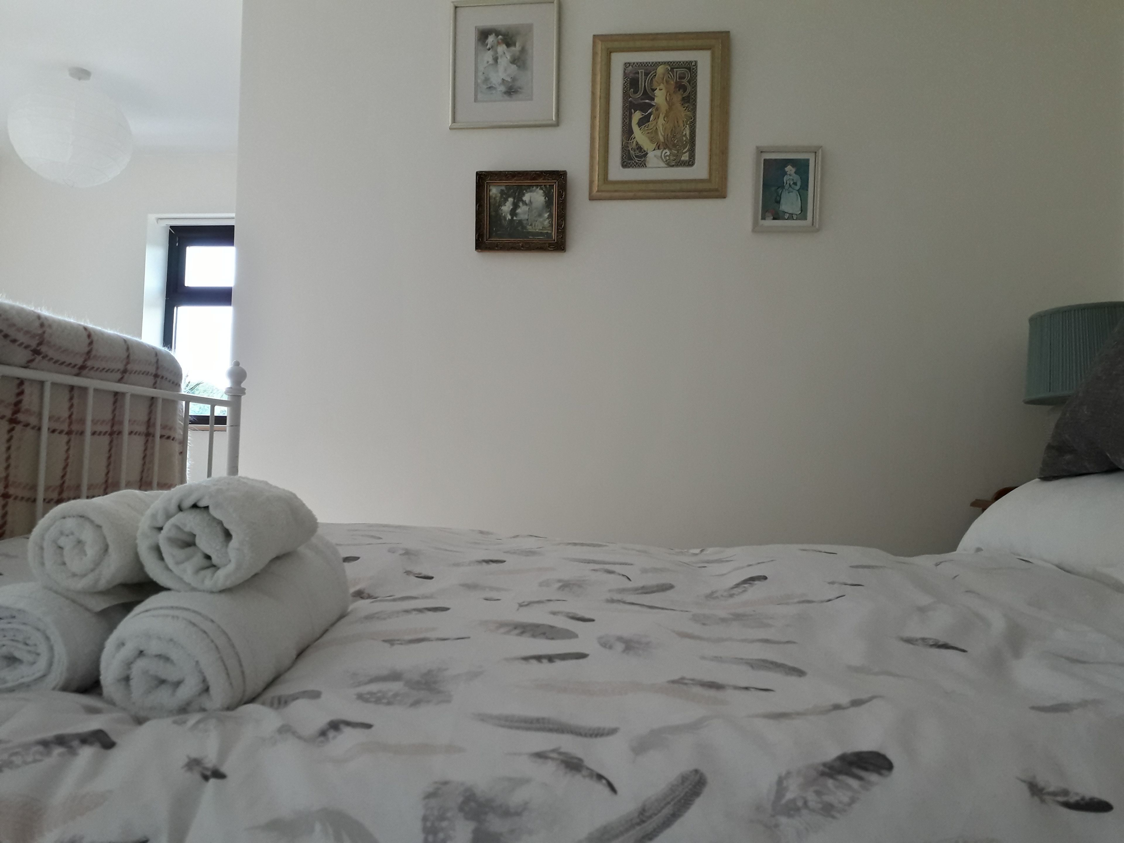 Uma cama bem arrumada com toalhas dobradas, uma janela com persianas e três quadros na parede.