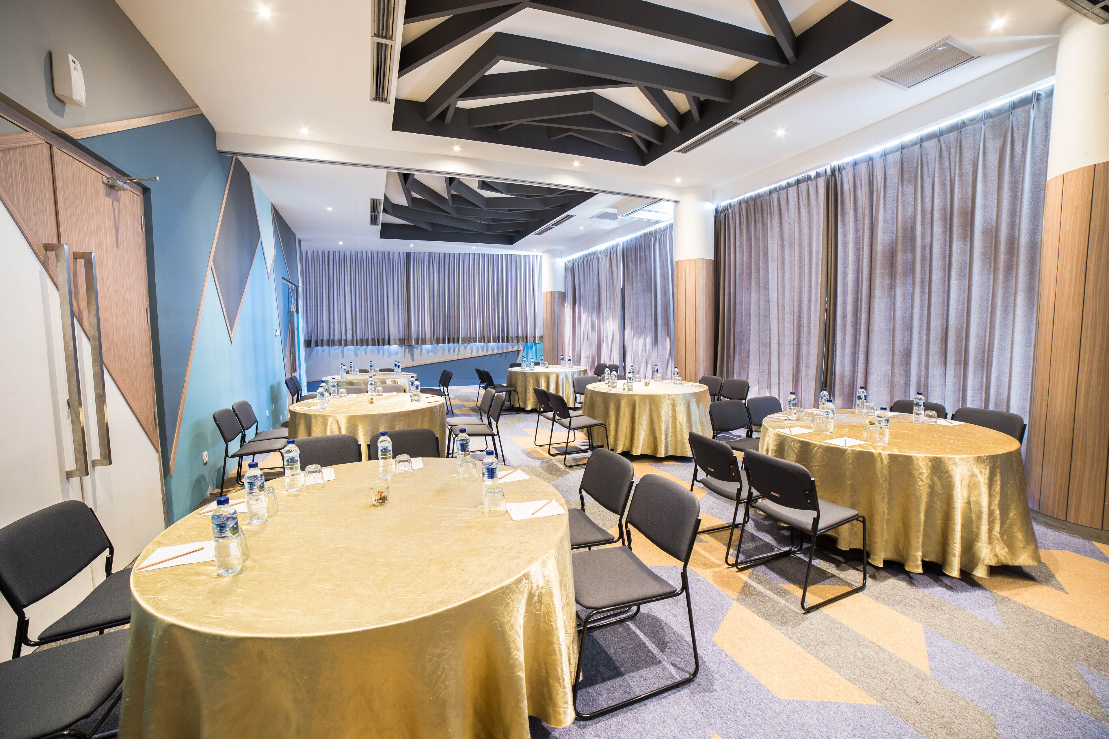 Sala de conferências com várias mesas, cadeiras e um design de teto moderno.