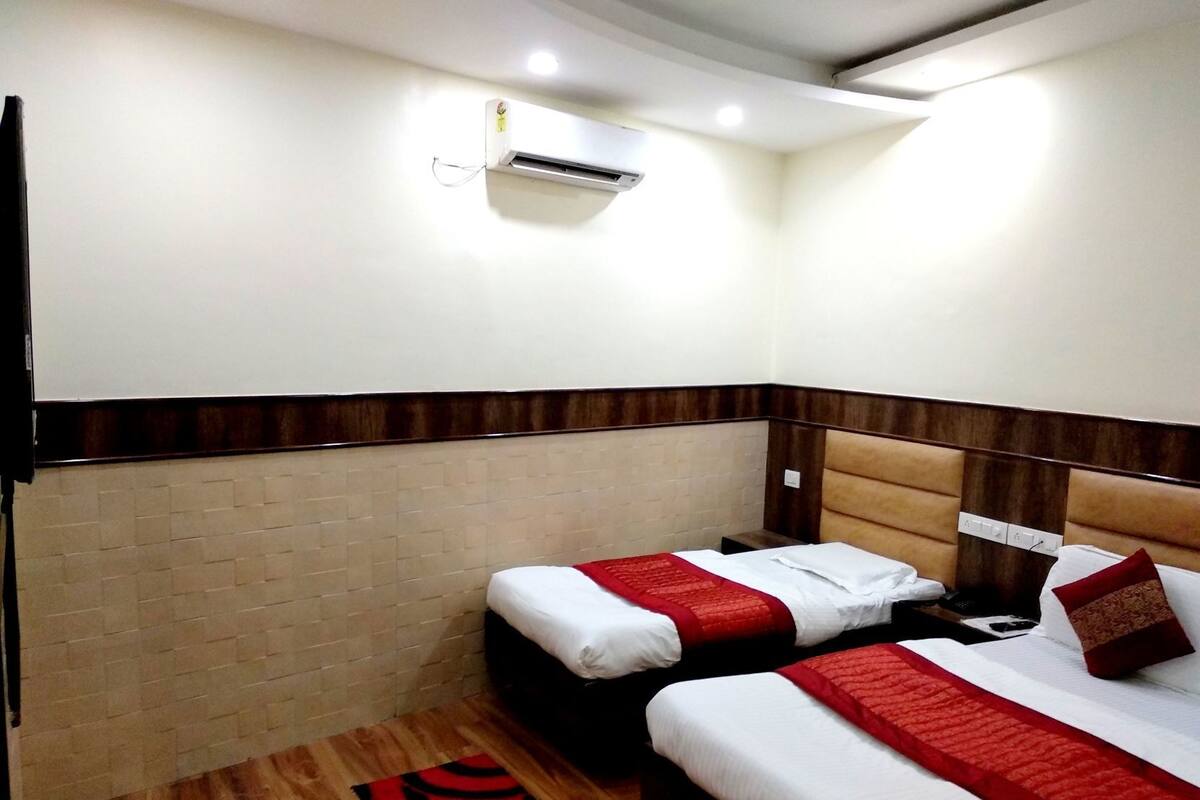 Quarto de hotel com duas camas, colcha vermelha e branca, piso de madeira, parede de tijolos e ar condicionado.