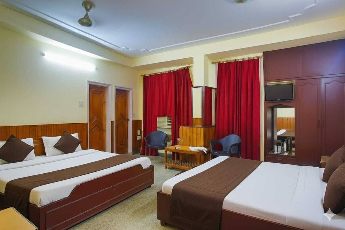 Quarto de hotel com duas camas, uma escrivaninha, uma cadeira, uma televisão e um guarda-roupa.