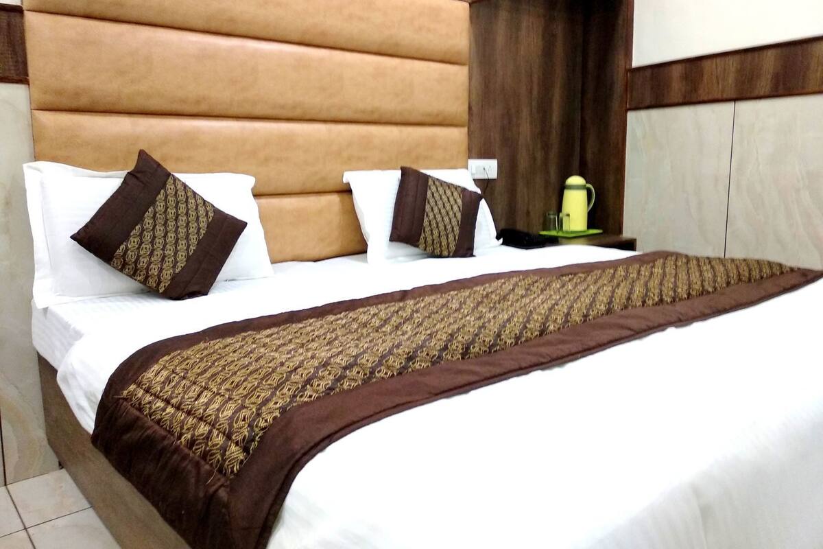 Quarto de hotel com uma cama grande, cabeceira de madeira e mesa de cabeceira com uma caneca amarela.