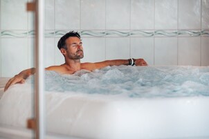 Um homem relaxando em uma banheira de hidromassagem com uma parede de azulejos ao fundo.