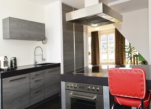 Cozinha moderna com exaustor de aço inoxidável, forno embutido e uma cadeira vermelha.