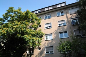 Um edifício de vários andares com diversas janelas, algumas com persianas, e uma antena parabólica na lateral.