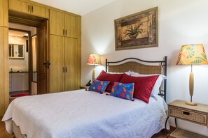 Quarto com cama grande, guarda-roupa de madeira, duas luminárias de cabeceira e um quadro pendurado na parede.