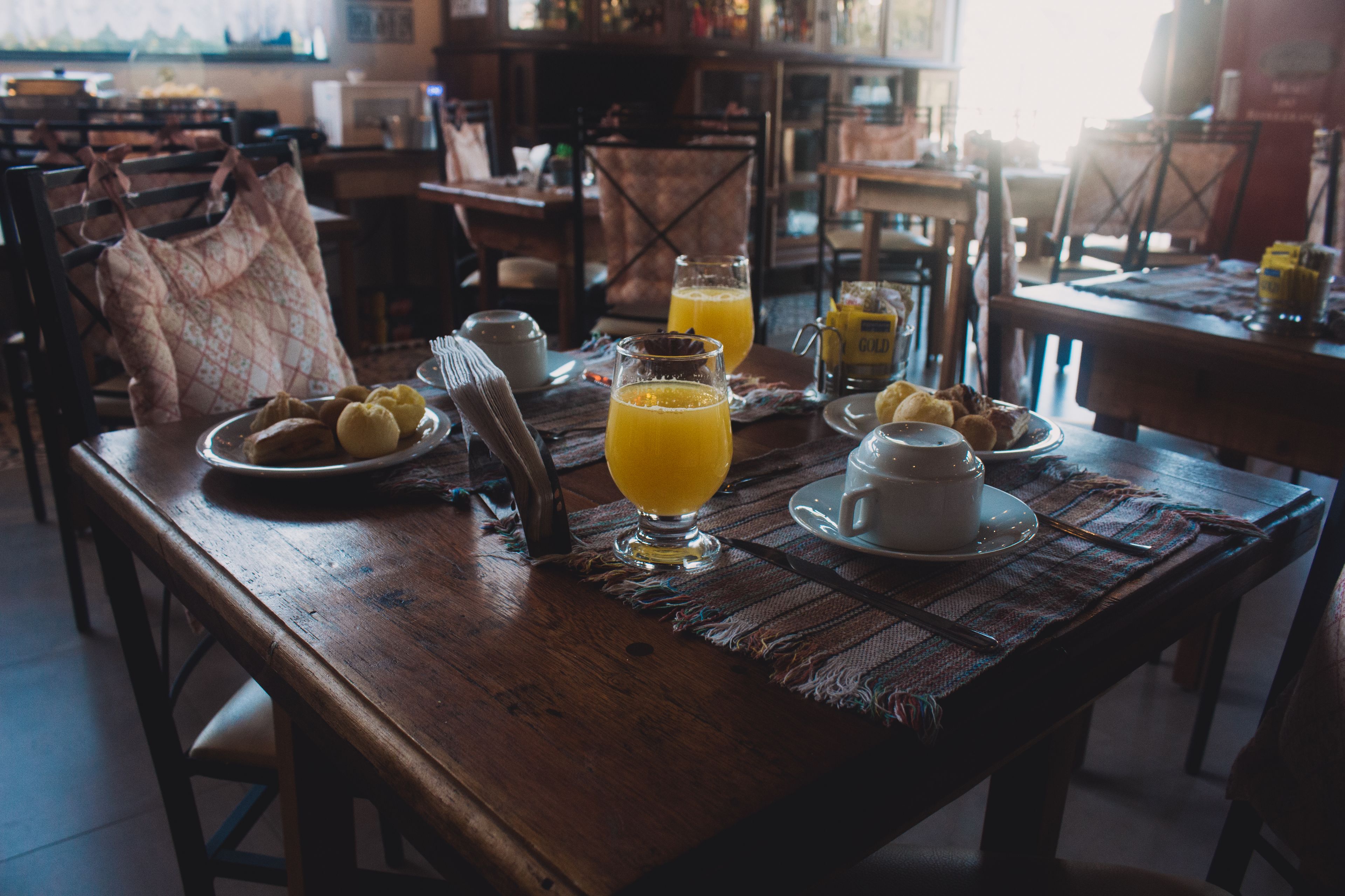 Uma mesa de jantar de madeira com pratos de comida, copos de suco de laranja e uma cafeteira.