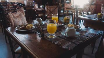 Uma mesa de jantar de madeira com pratos de comida, copos de suco de laranja e uma cafeteira.