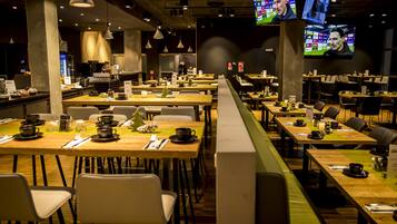 Um restaurante moderno com várias mesas e cabines, equipado com televisores de tela plana exibindo eventos esportivos.