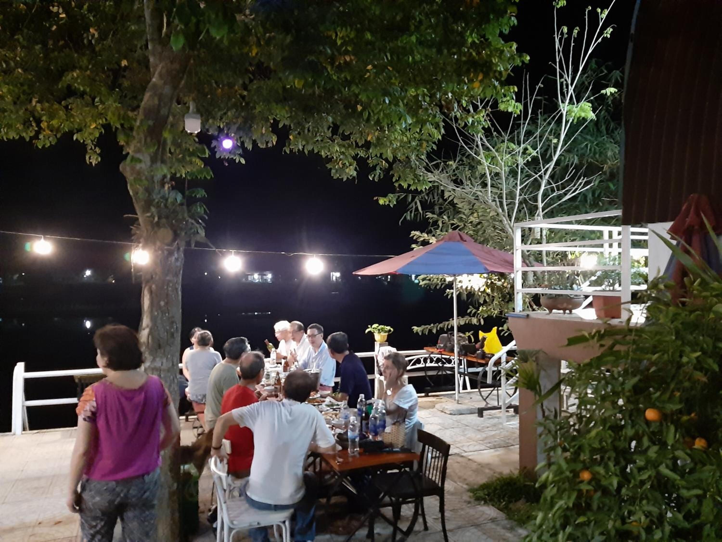 Uma área de refeições ao ar livre com mesas e cadeiras, cercada por árvores e um corrimão.