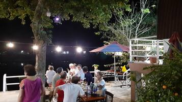 Uma área de refeições ao ar livre com mesas e cadeiras, cercada por árvores e um corrimão.