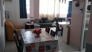 Uma área de refeições com uma mesa coberta por uma toalha com tema de frutas, um sofá e uma janela com cortinas.