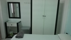 Quarto com cama, mesa de cabeceira, espelho, guarda-roupa e uma pequena lixeira.