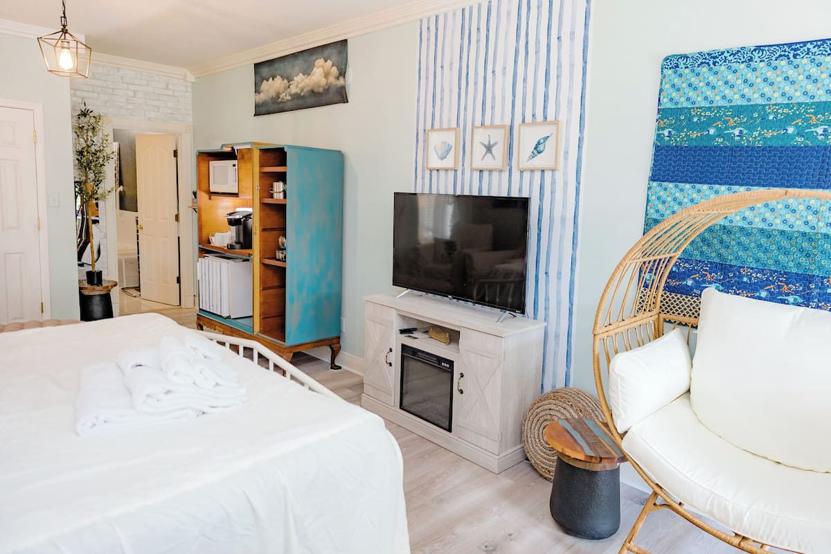 Quarto com cama, televisão, guarda-roupa e uma cadeira de vime.